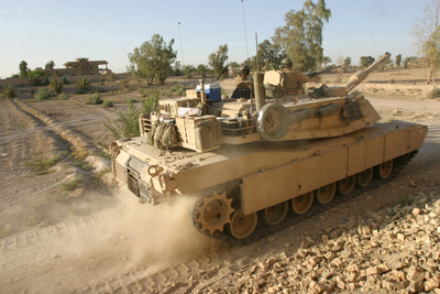 An M-1A1 Abrams tank kicks up dust as it moves into position.
