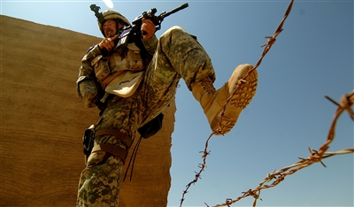 A U.S. Army soldier steps over strands of barbed wire.