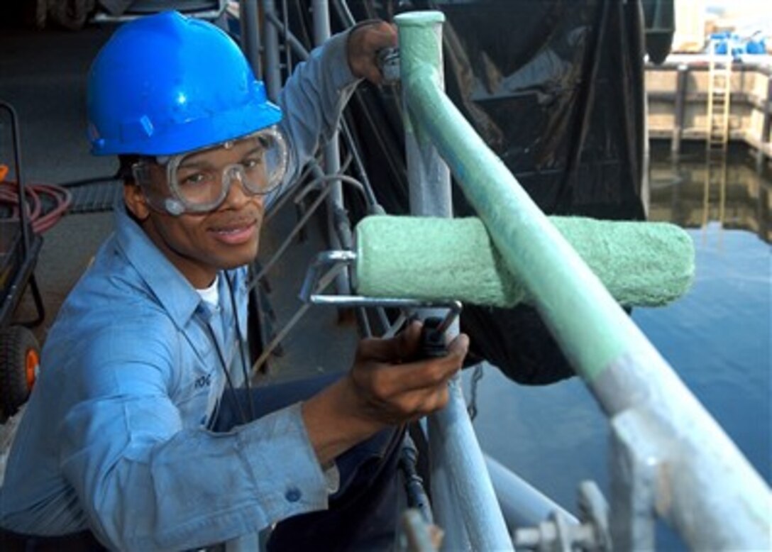 Navy Seaman Michael Rogers applies primer to a railing.