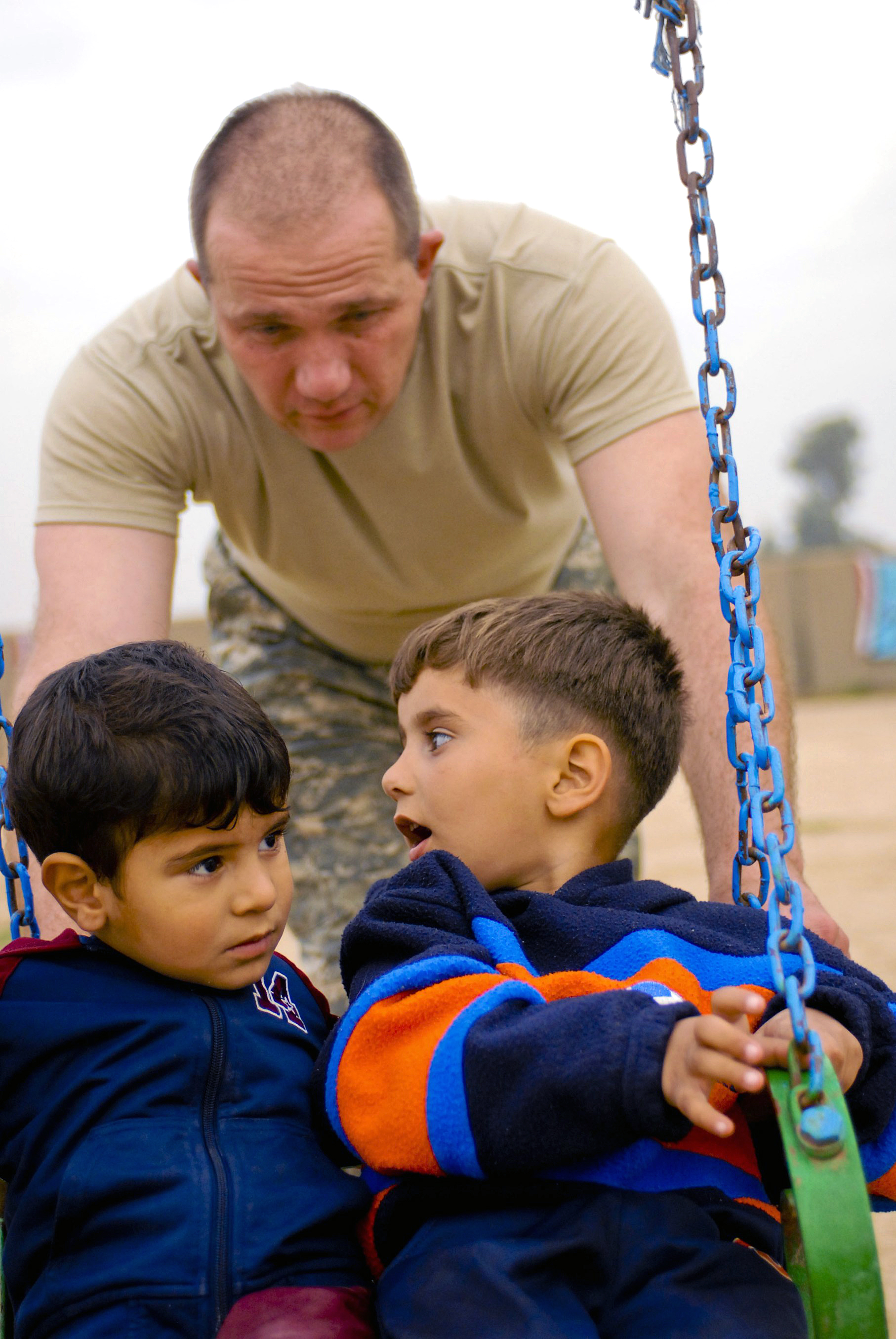 U.S. Army Sgt. Maj. Wayne Simmons pushes two boys on a swing during a ...