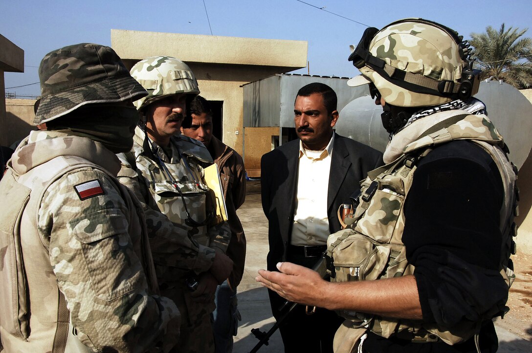 Polish army soldiers and an Iraqi contractor discuss business about a ...