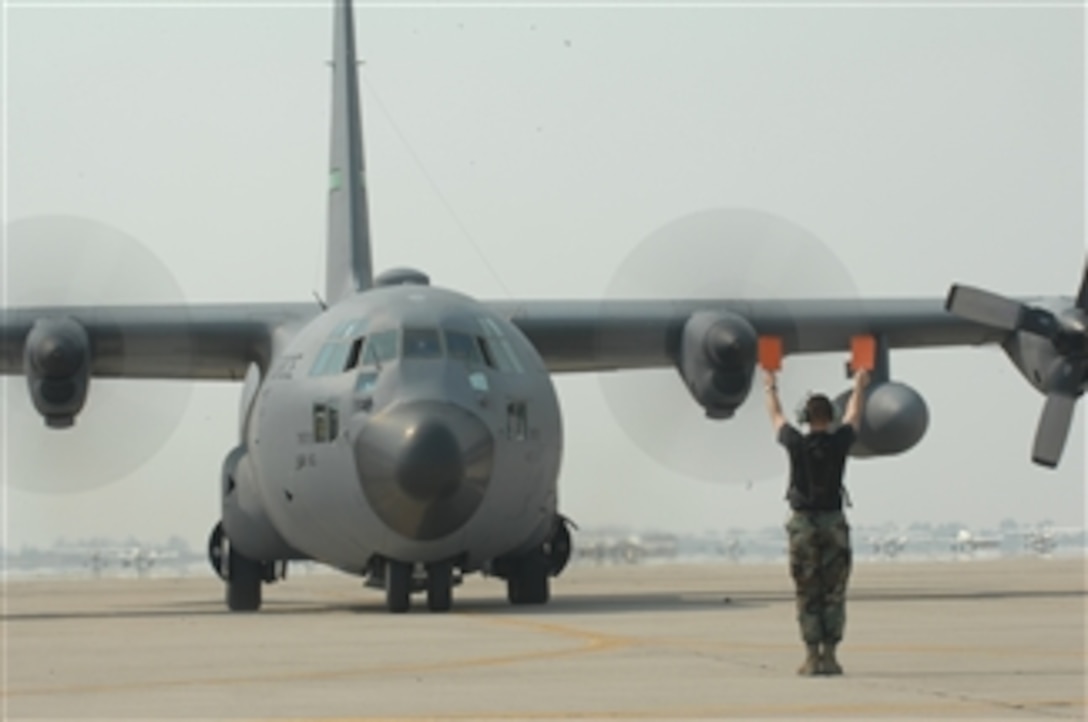 A U.S. Air Force crew chief guides a C-130 Hercules aircraft.