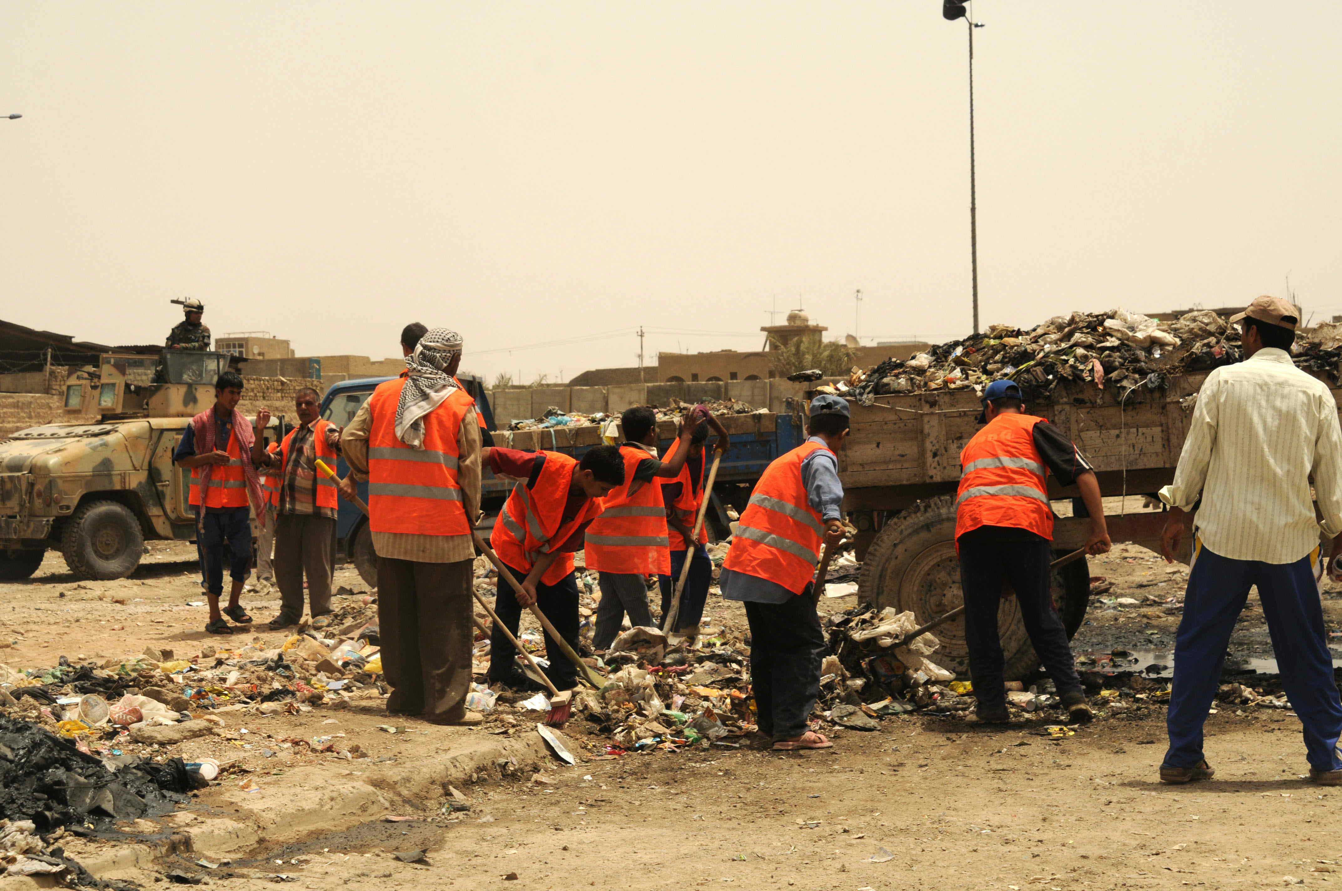 Iraqi workers shovel rubble and debris into a wagon as part of an ...
