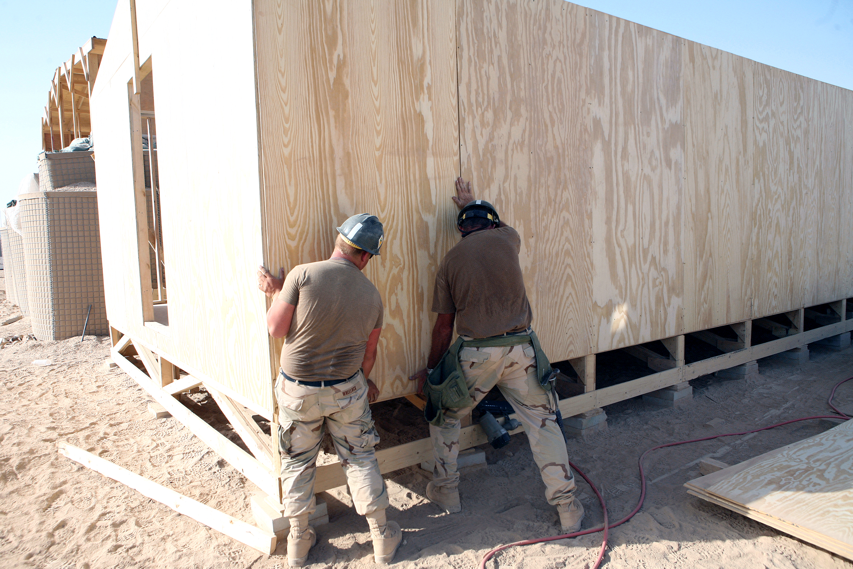 U.S Navy Seabees construct the wall on a hut to house Marines on a ...