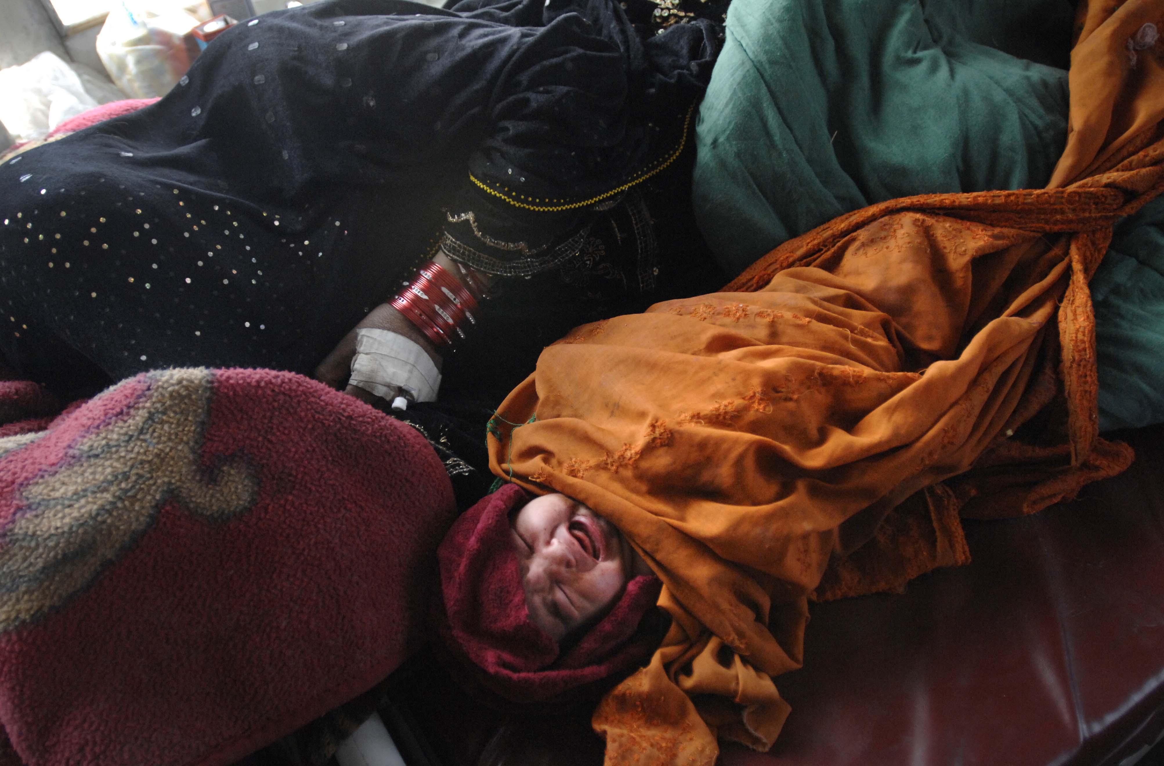 A mother rests on the bed, wrapped in her traditional Afghan burka ...