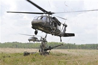 U.S. Army soldiers connect lifting slings between M-119A2 lightweight ...