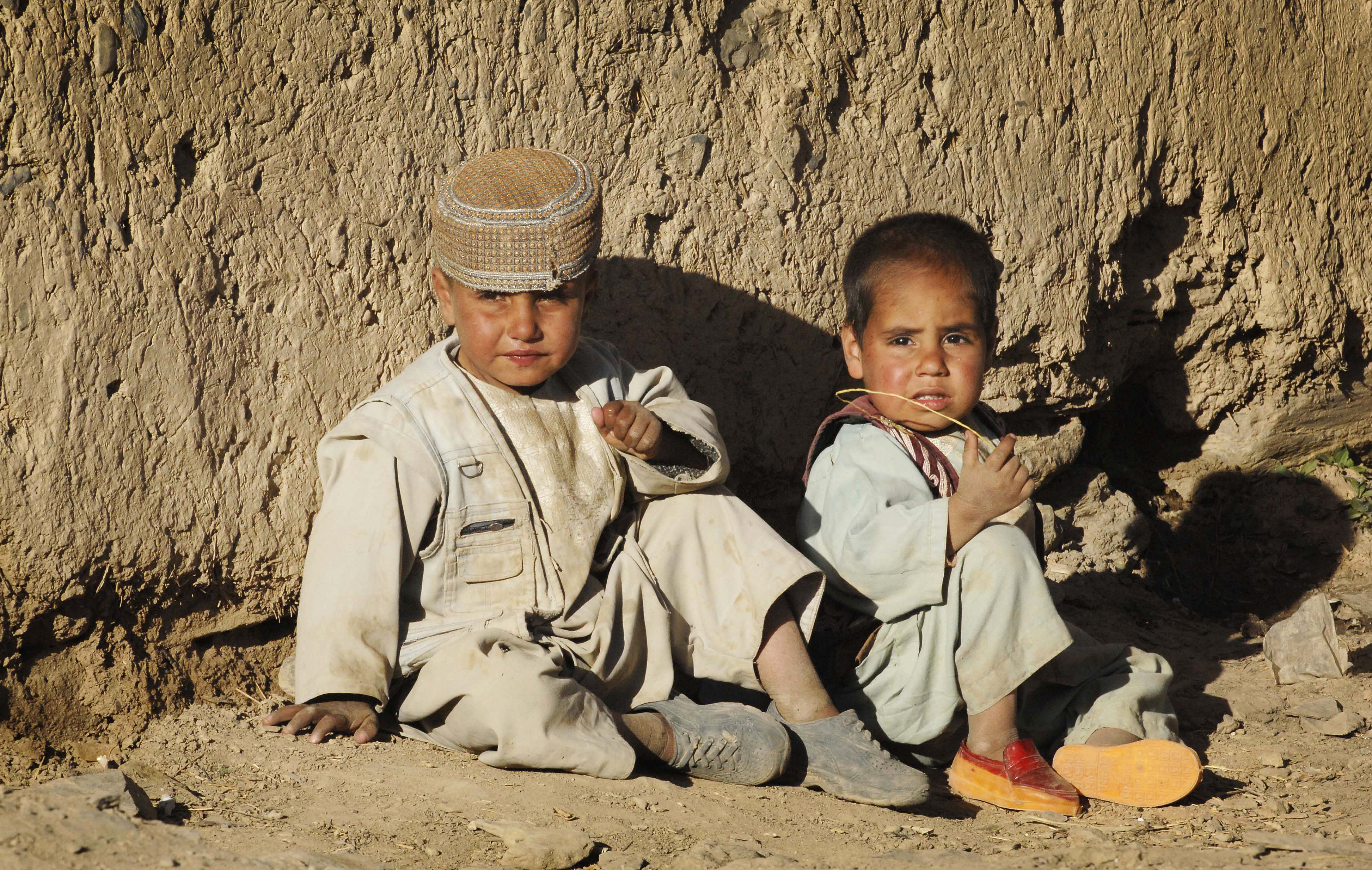 Two small boys sit in the evening sun next to their qalat in a village ...
