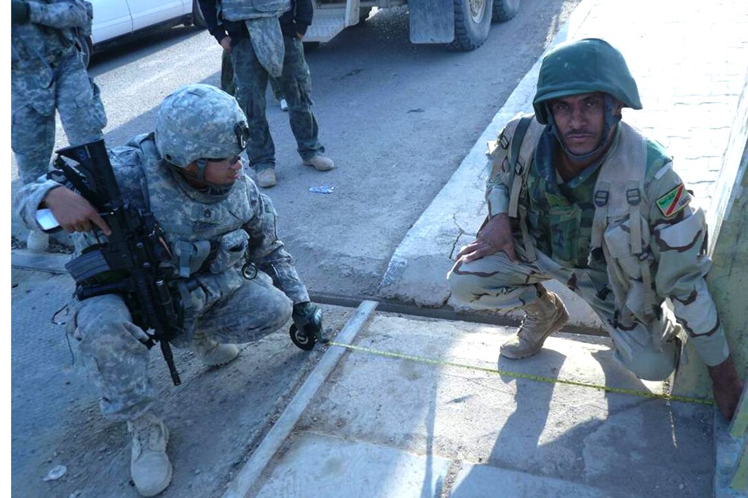Army Staff Sgt. Fabio Herrera takes measurements with an Iraqi soldier ...