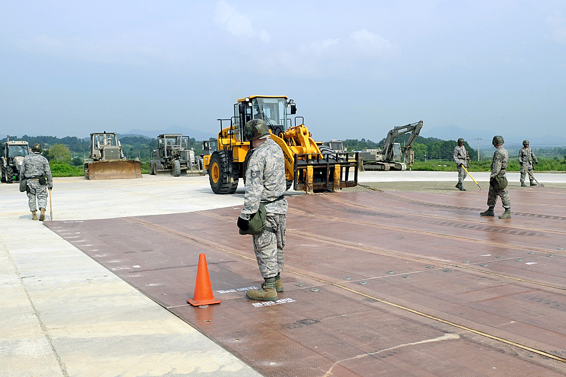 U.S. Air Force airmen stand on a folded fiberglass mat as it is moved ...
