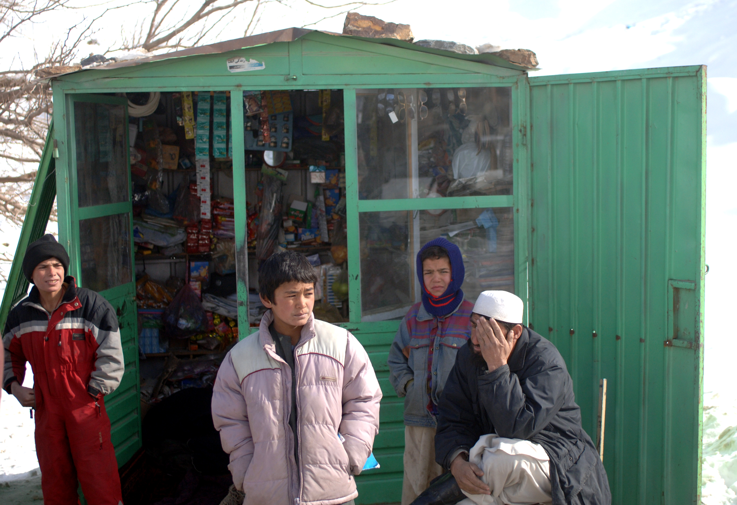 An Afghan man and some children sit in front of their store on the road ...