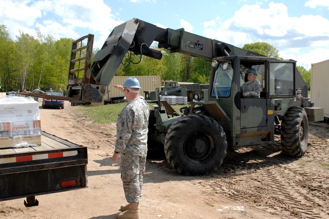 U.S. Army soldiers use a large forklift to move building material while ...