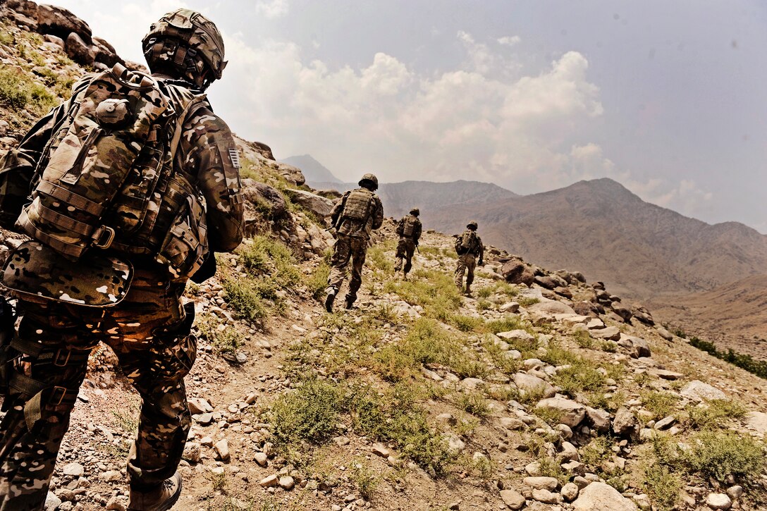U.S. Army soldiers hike up a hillside after visiting a high school ...
