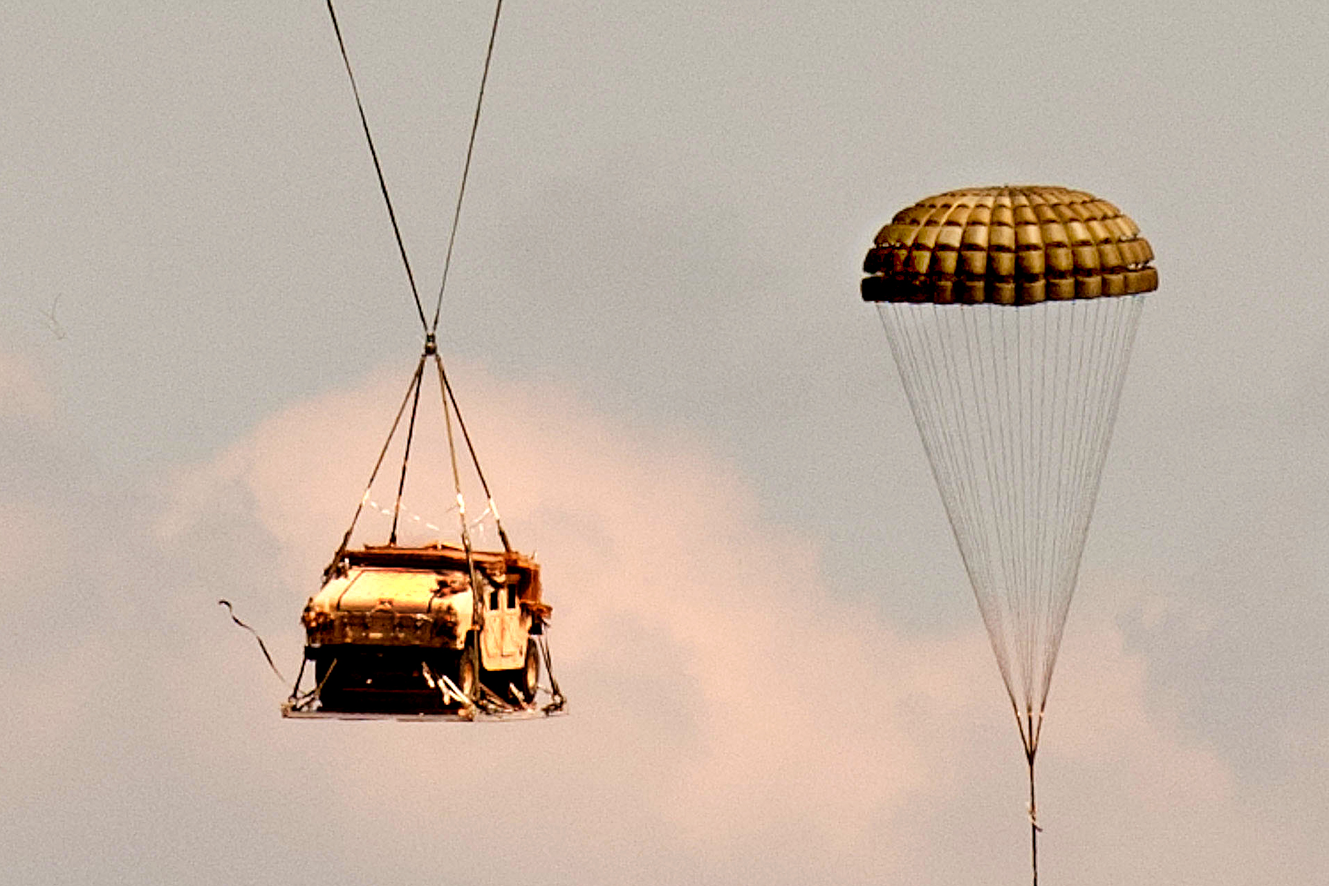 A Humvee attached to a parachute falls to the ground during an airborne ...