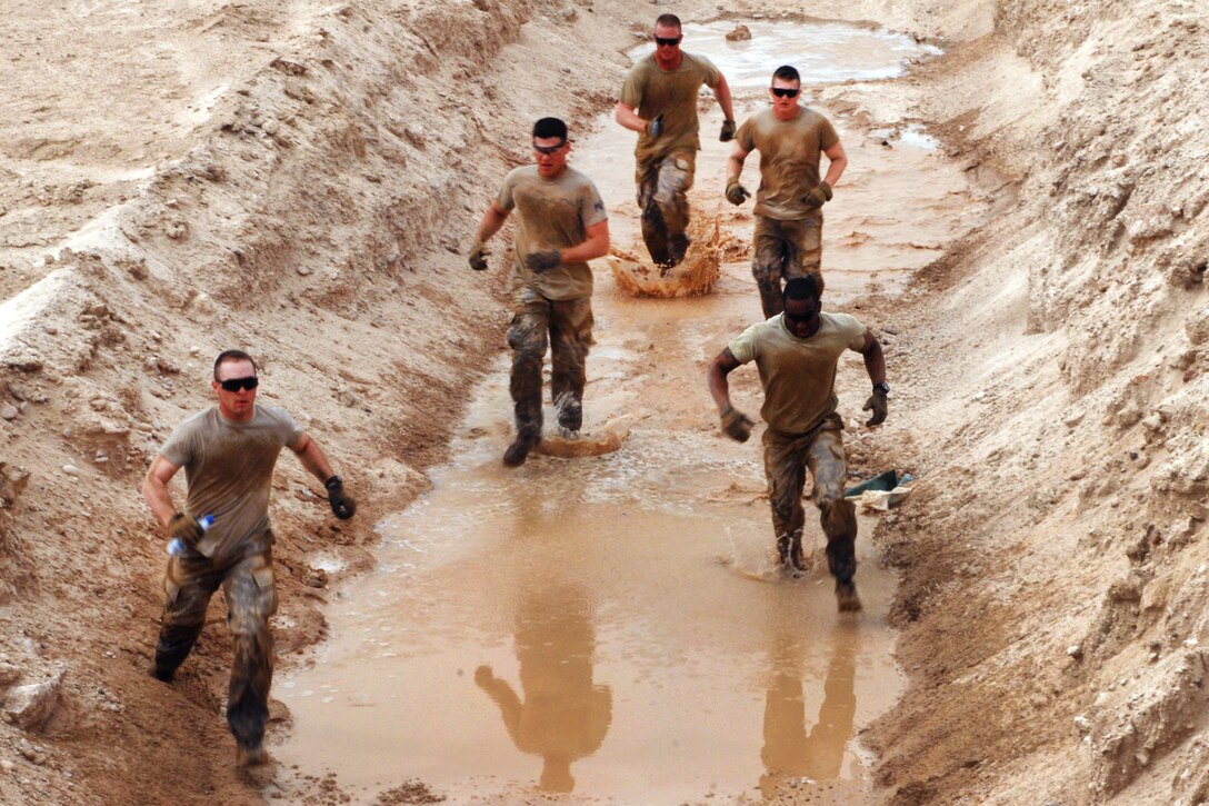 U.S. soldiers run through a muddy trench during the Tough Mudder ...