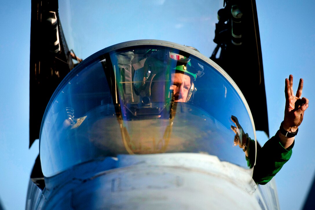 U.S. Navy Petty Officer 2nd Class Jack McMurrain signals to a plane ...