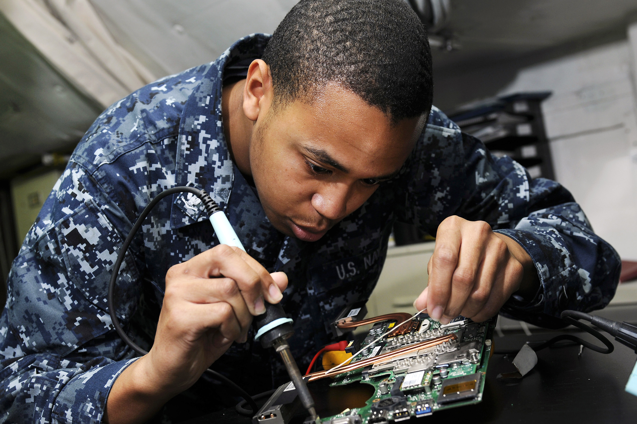 U.S. Navy Petty Officer 3rd Class Rowdy Rasmus solders computer ...