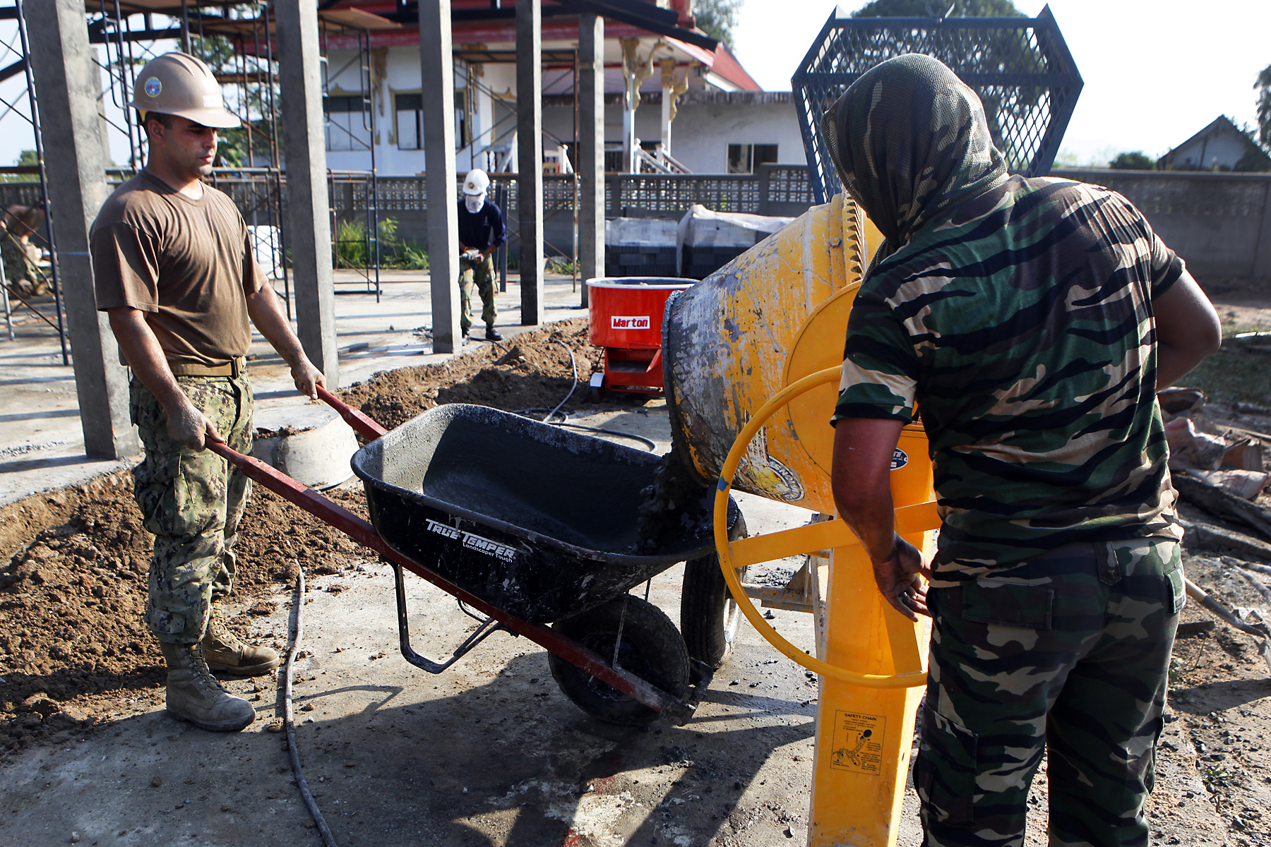 U.S. Navy Seabee Robert Axley, left, and a Thai sailor pour concrete into a wheel barrow during ...