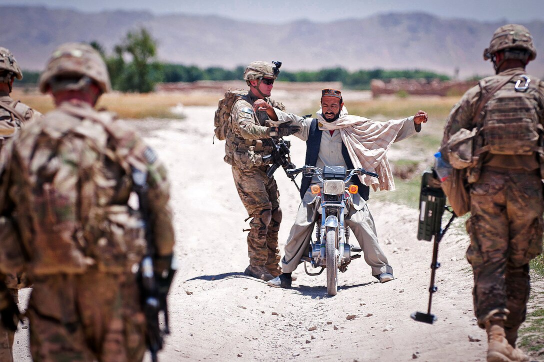 U.S. Army paratroopers search a passerby while sweeping a road for improvised explosive devices ...