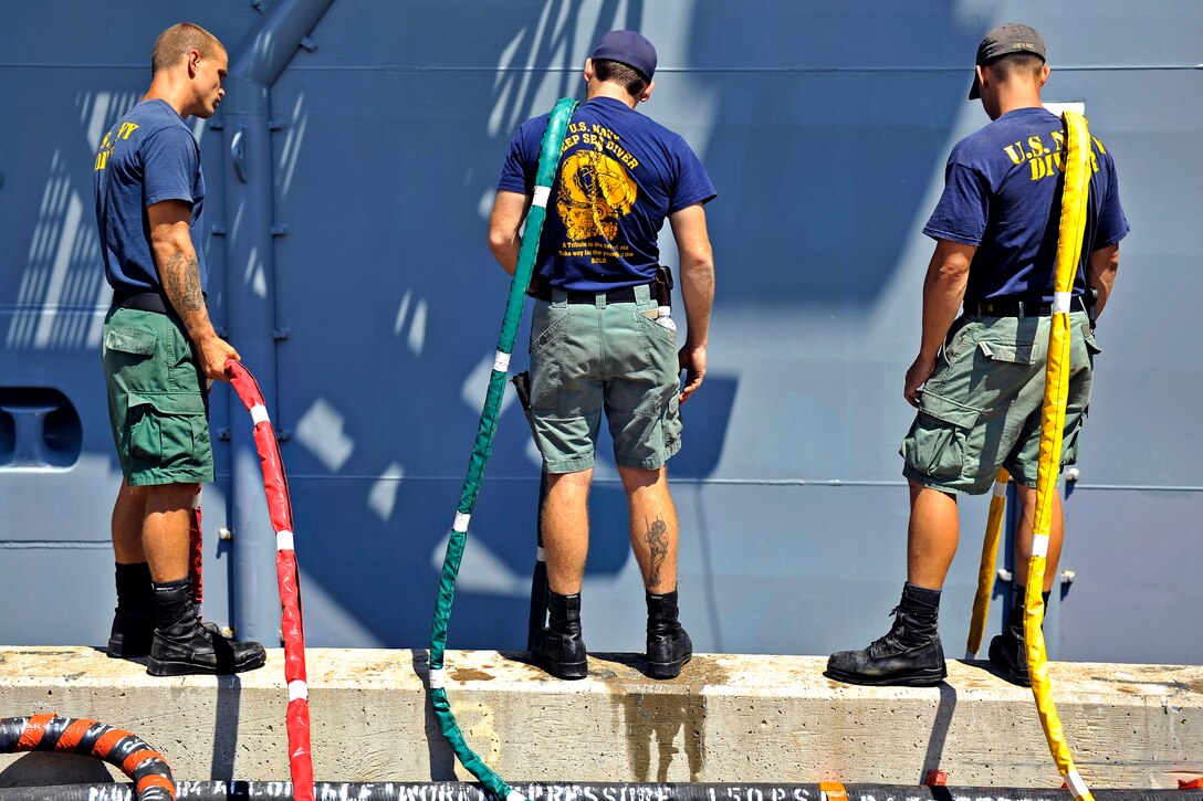 Navy divers monitor air lines for other divers performing underwater ...