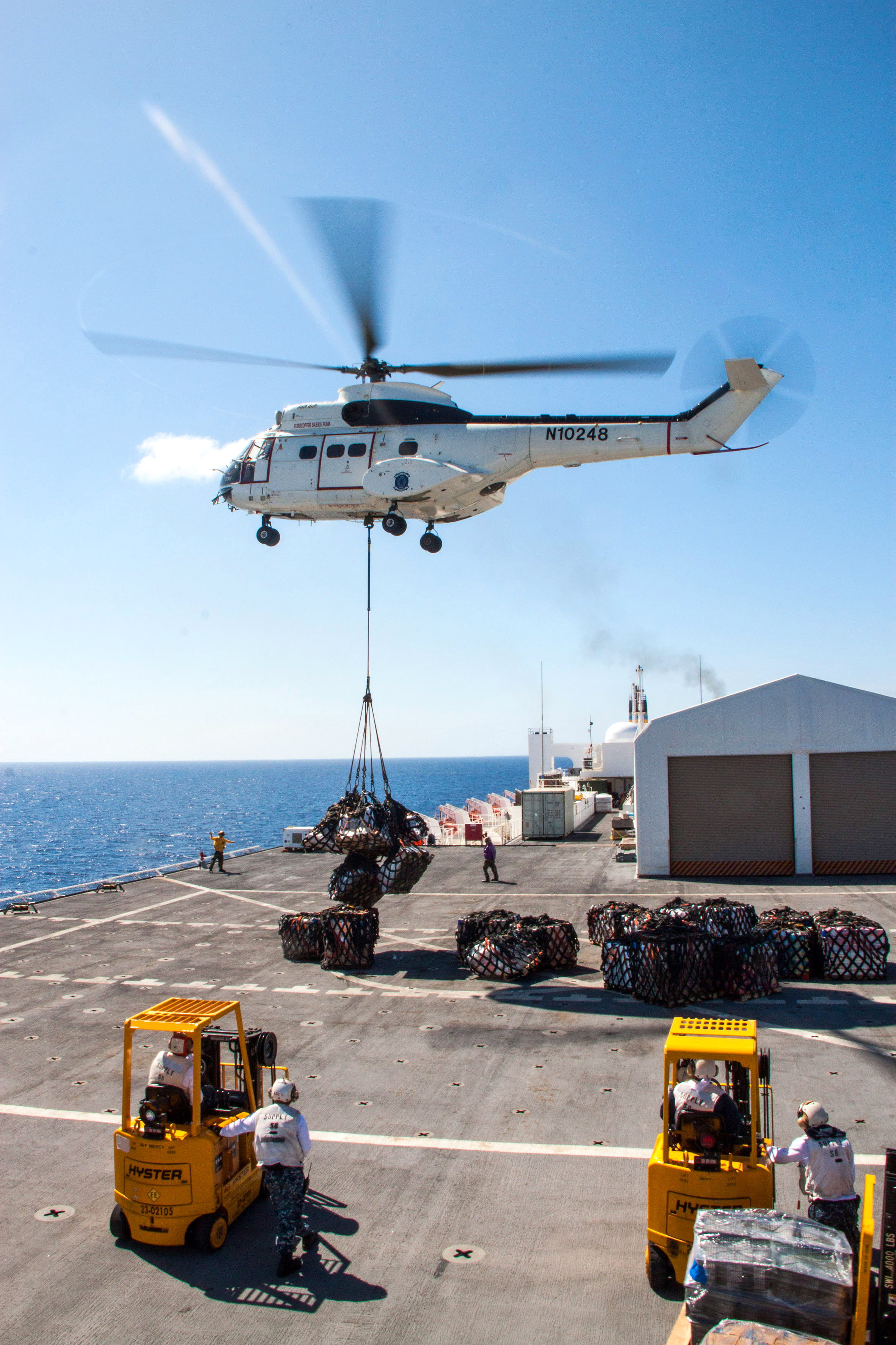 U.S. Navy forklift teams stand by as a SA-330J Puma helicopter delivers ...
