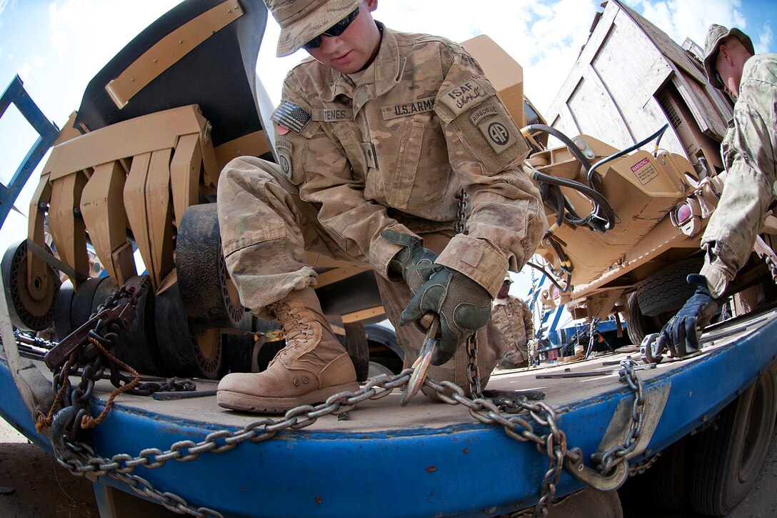 U.S. Army Spc. Alexander Istenes tightens a chain on a truck holding ...