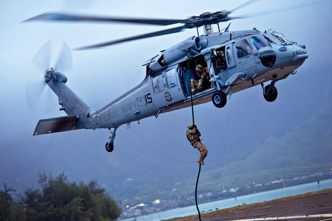 A U.S. sailor fast ropes out of a U.S. Navy MH-60S Night Hawk ...