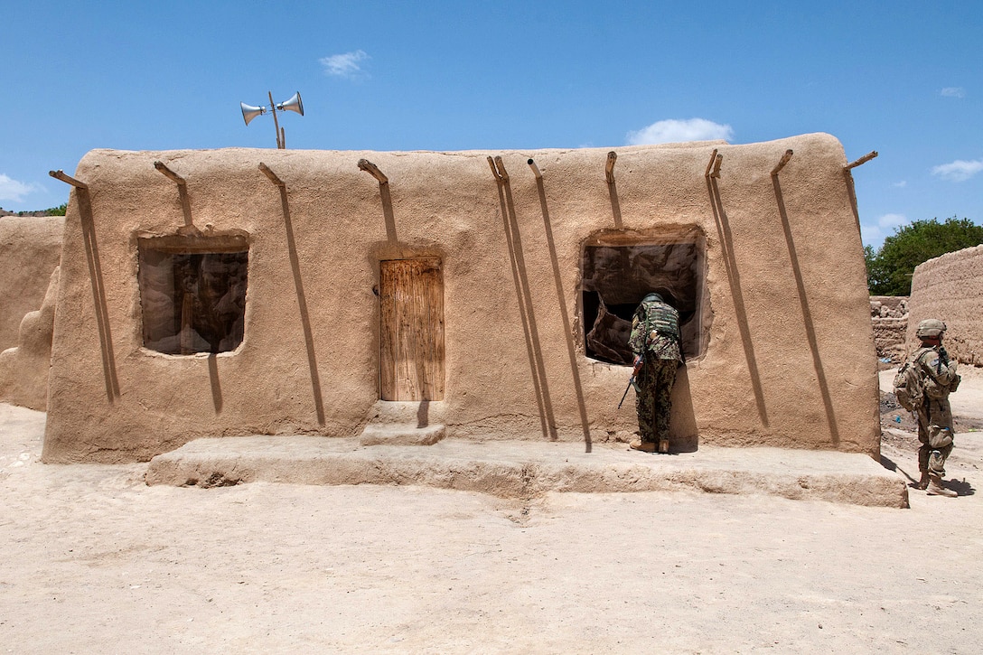 An Afghan soldier inspects inside of a mosque while a U.S. paratrooper ...