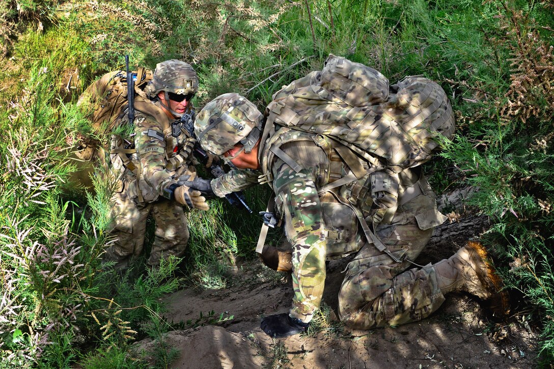 A U.S. soldier helps U.S. Army Cpl. John Hately up a muddy hill during ...