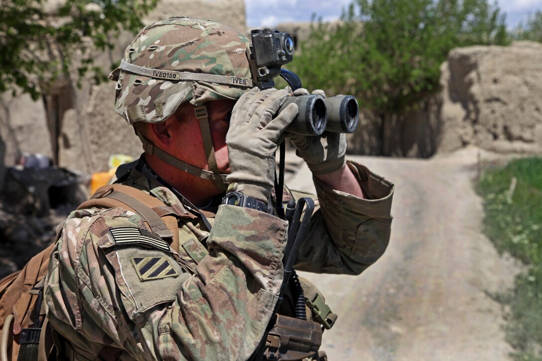 U.S. Army Staff Sgt. Nicholas Ives looks through his binoculars at the ...