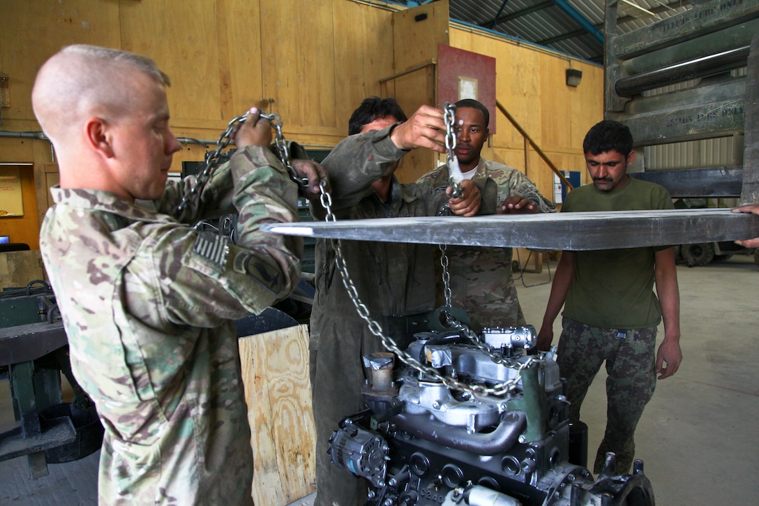 U.S.and Afghan soldiers lift an engine from a crane at the motor pool ...