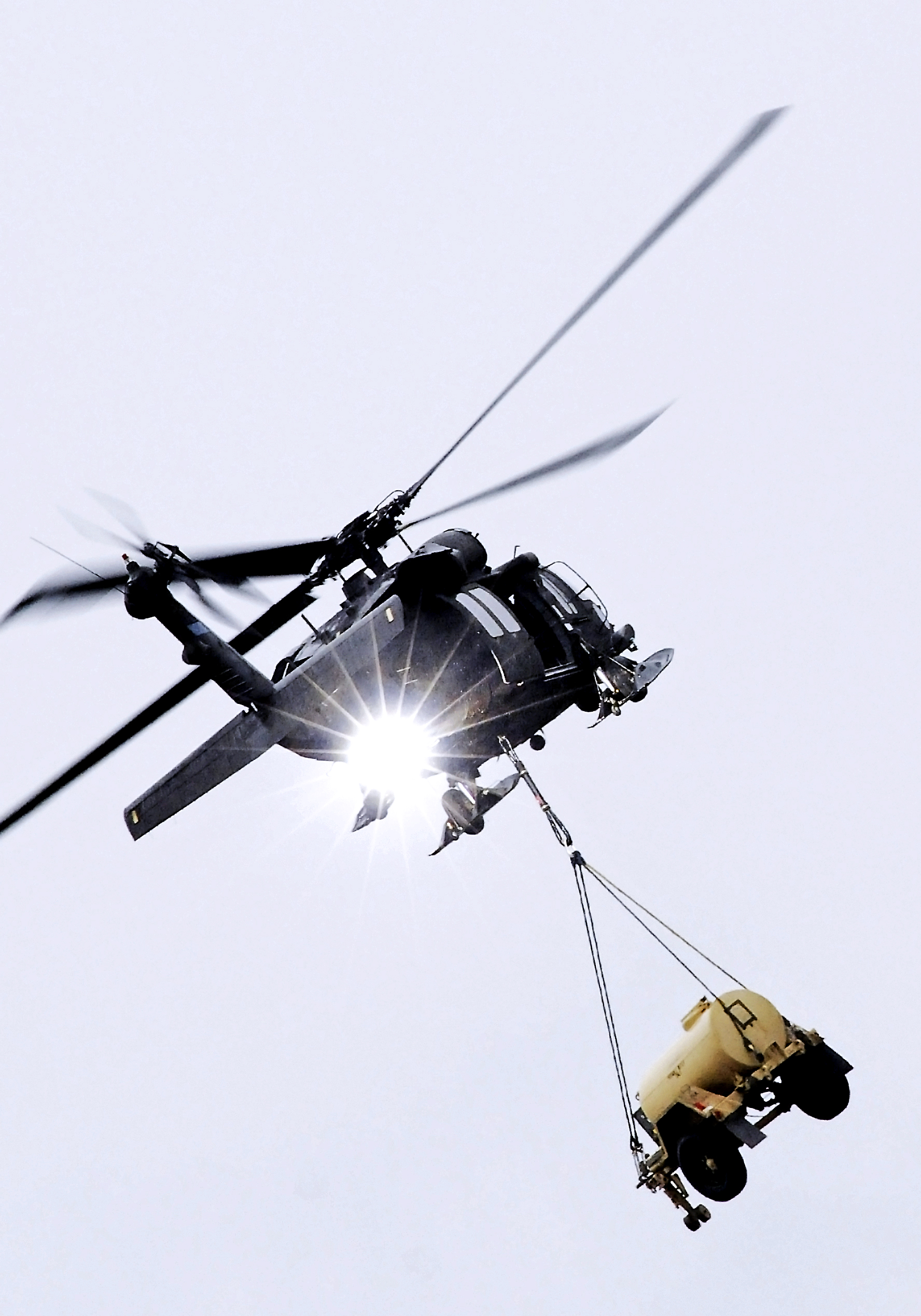 A UH-60L Black Hawk helicopter carries a water trailer away during ...