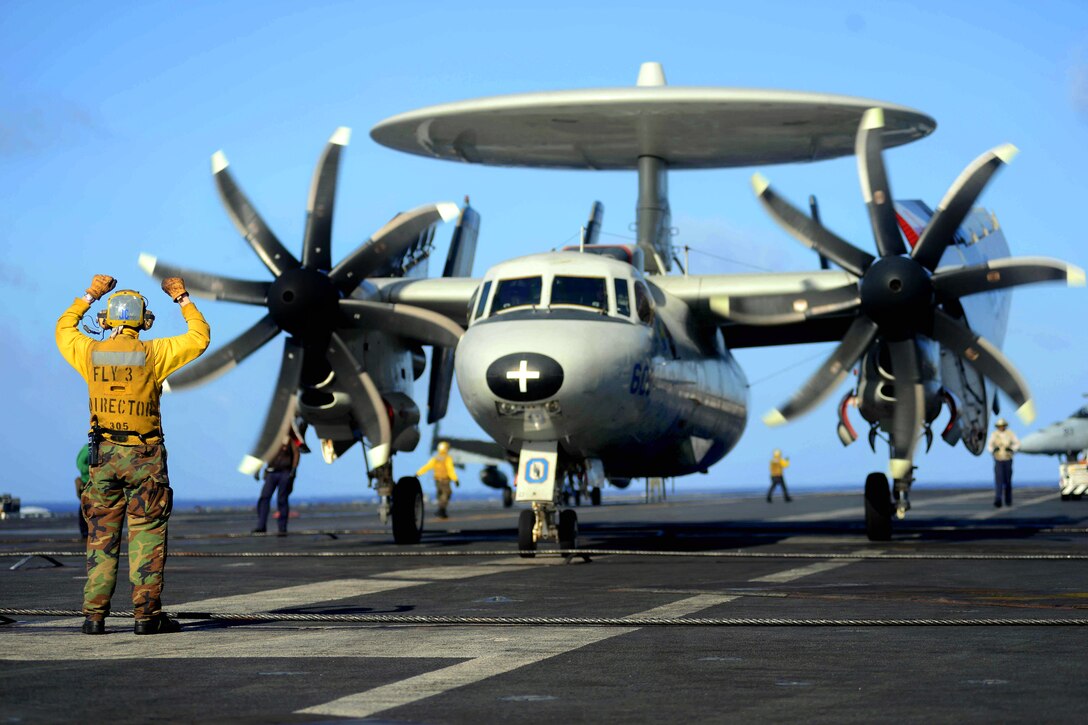 U.S. Navy Petty Officer 3rd Class Otis Insley directs an E-2C Hawkeye ...