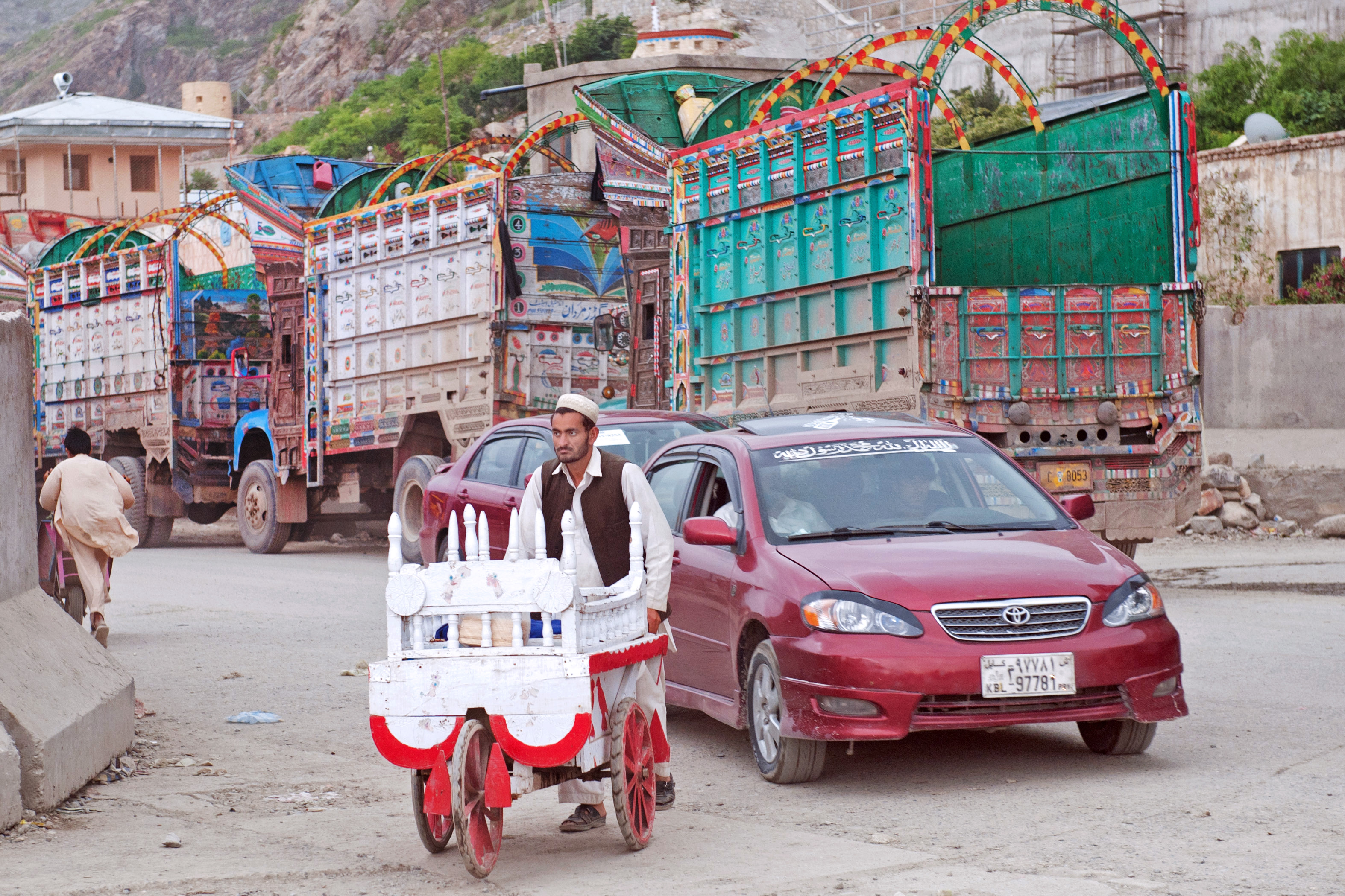 An Afghan man pushes a cart while vehicles approach the customs ...