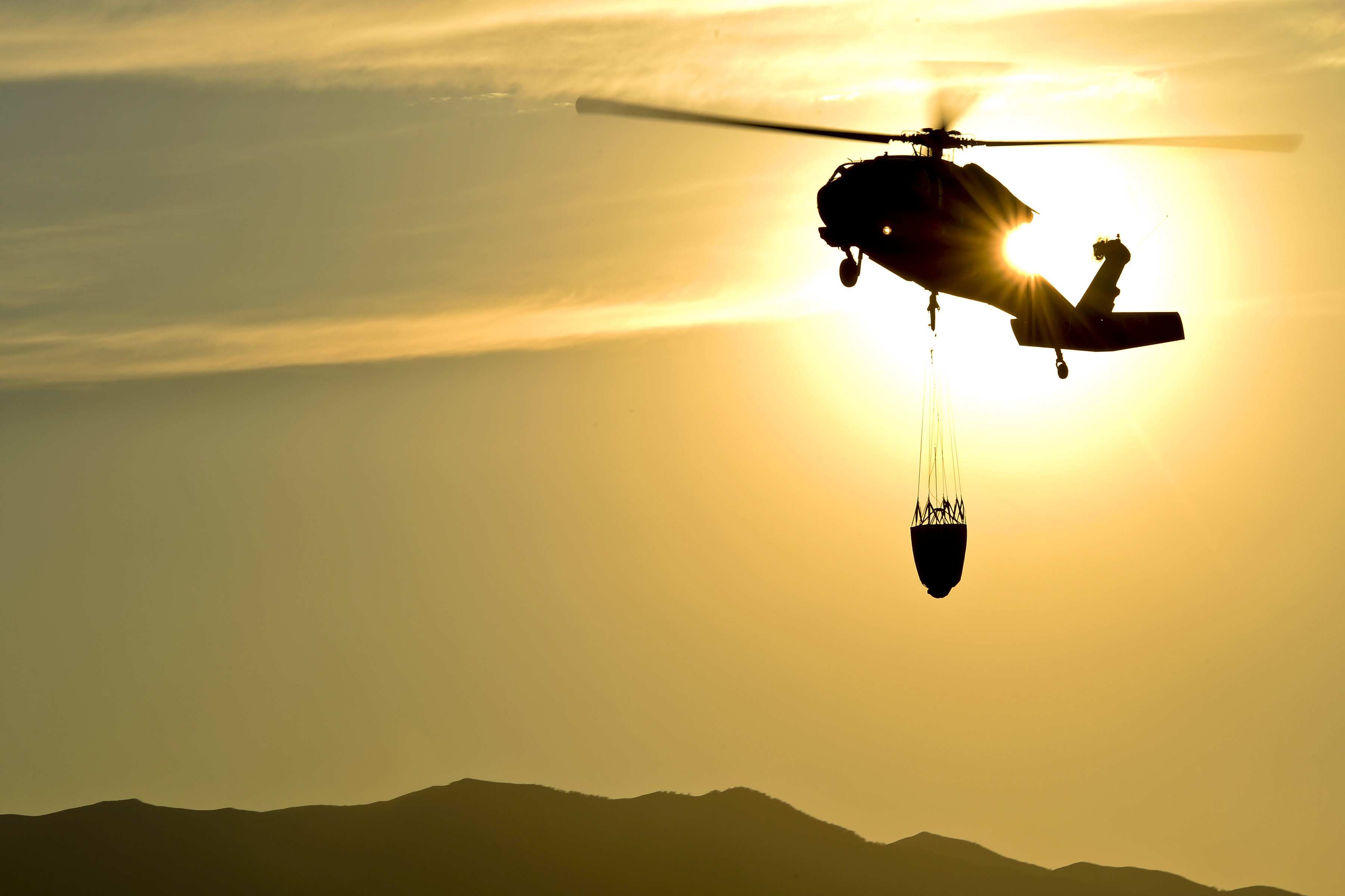 An Army UH-60 Black Hawk helicopter is silhouetted with a Bambi bucket ...