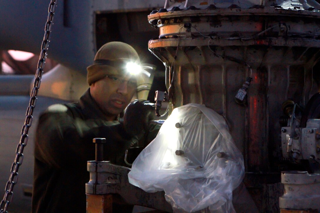 U.S. Marine Corps Cpl. Jose Espitia uses a headlamp to see while replacing a gear inside the ...