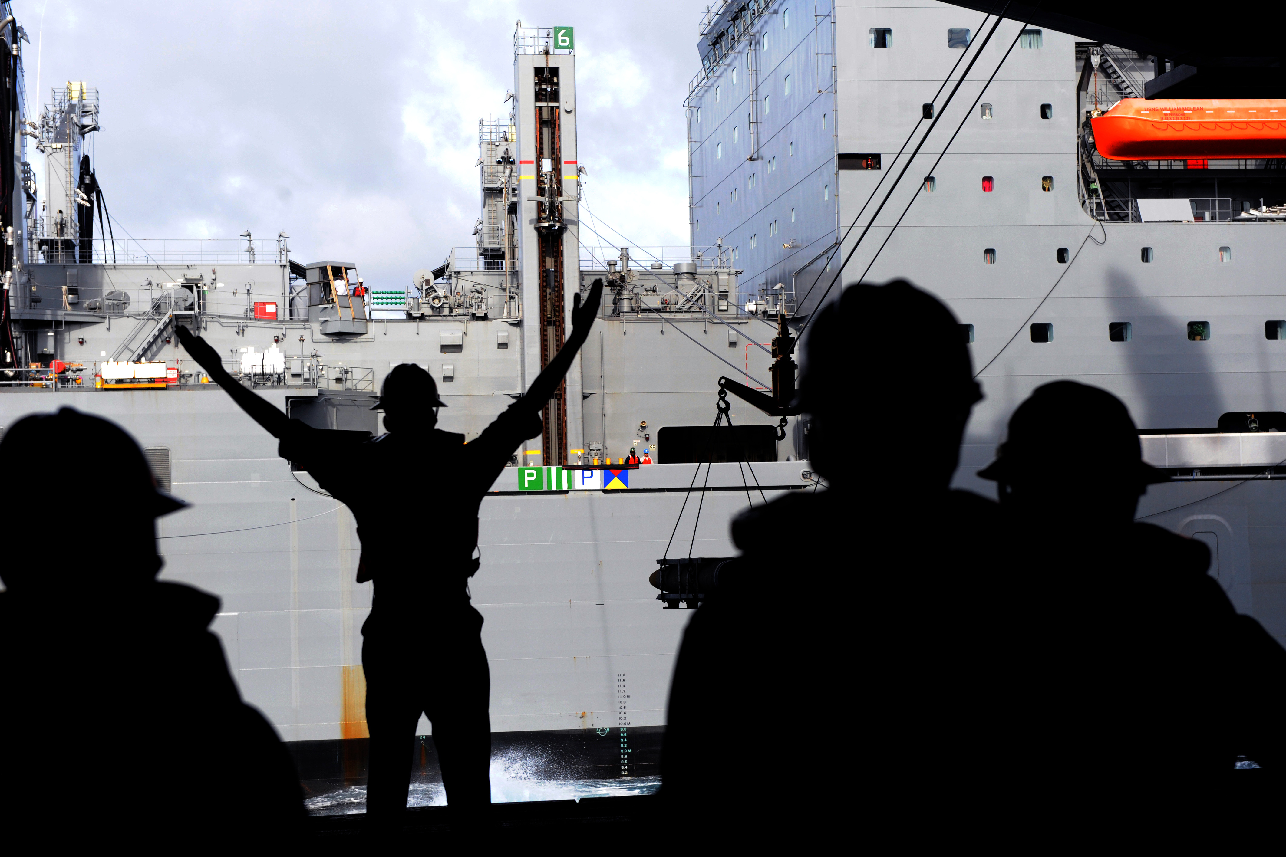 U.S. Navy Petty Officer 1st Class Stephen Markman signals to personnel ...