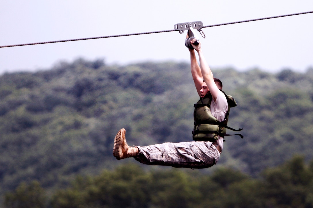 An Army cadet slides along a rope over the water obstacle during a ...