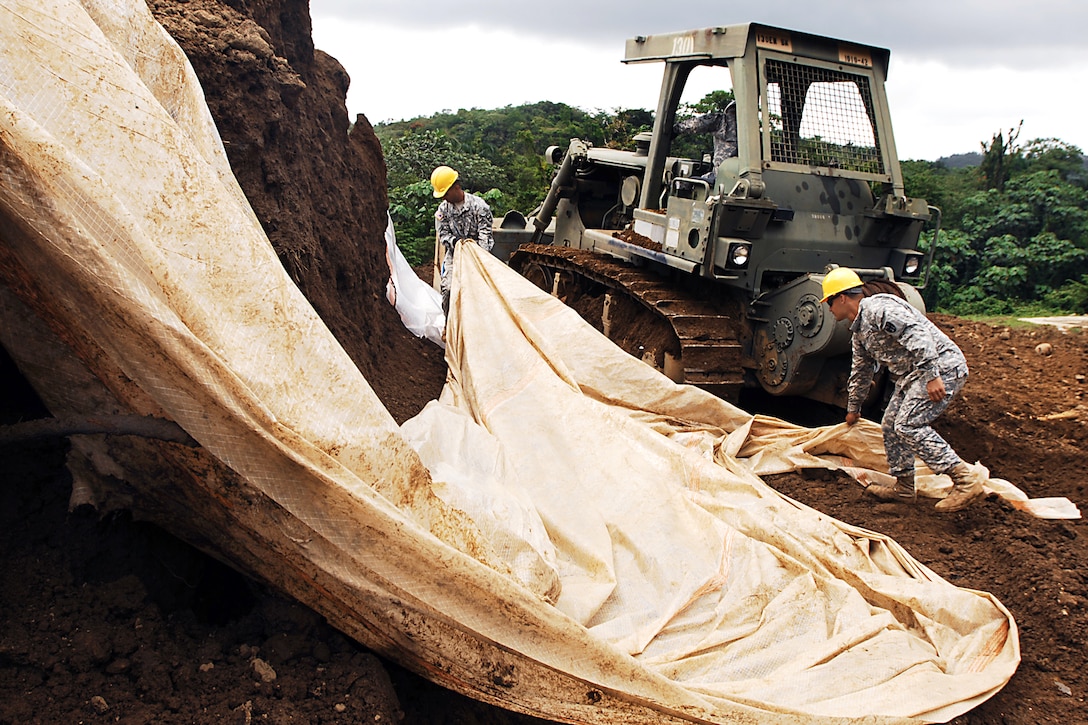 Soldiers use a plastic tarp to cover the top soil they were working ...