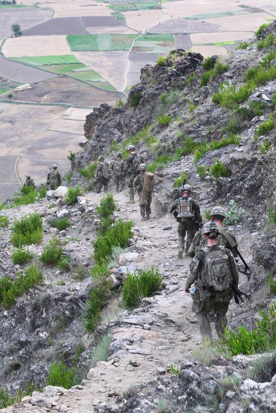 U.S. soldiers patrol down a mountainside and into a valley during a ...