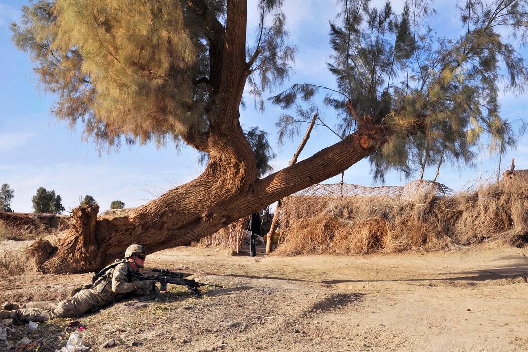 A U.S. soldier takes cover near a tree while providing security outside ...