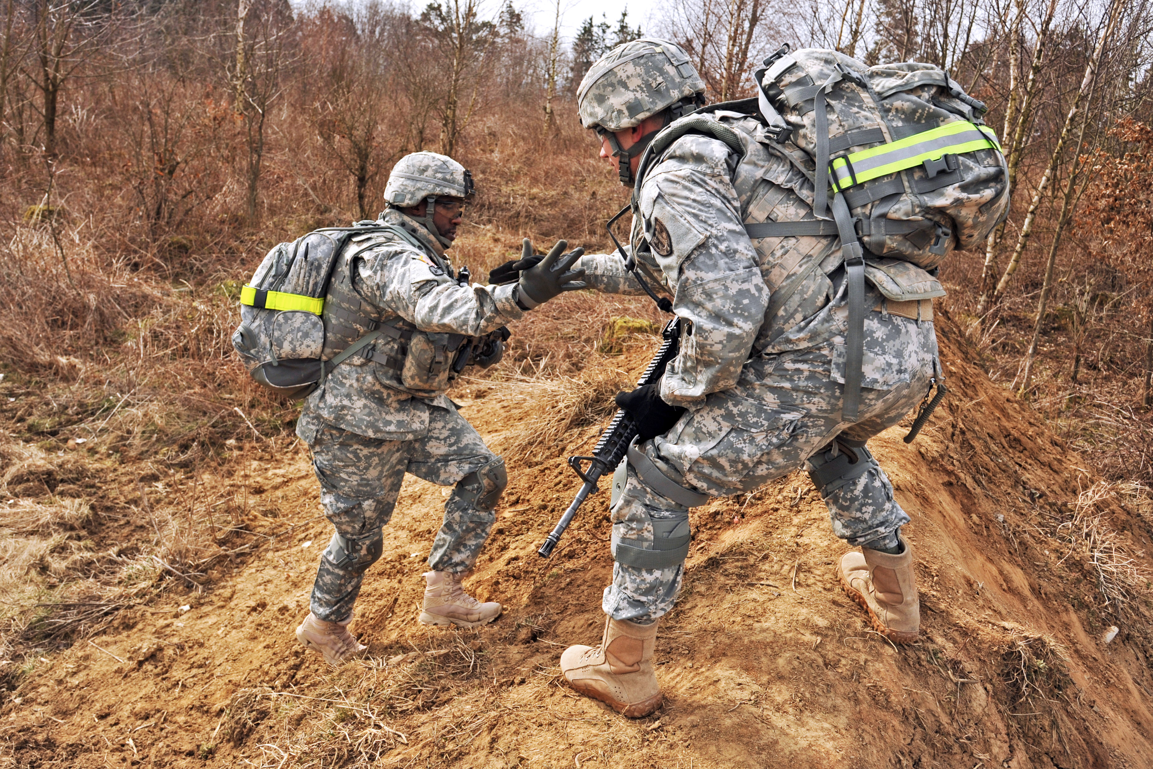 A U.S. soldier helps another soldier get over a berm obstacle on a ...