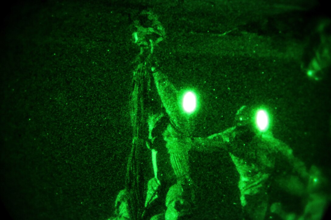 As seen through a night-vision device, U.S. soldiers hook up a cable ...