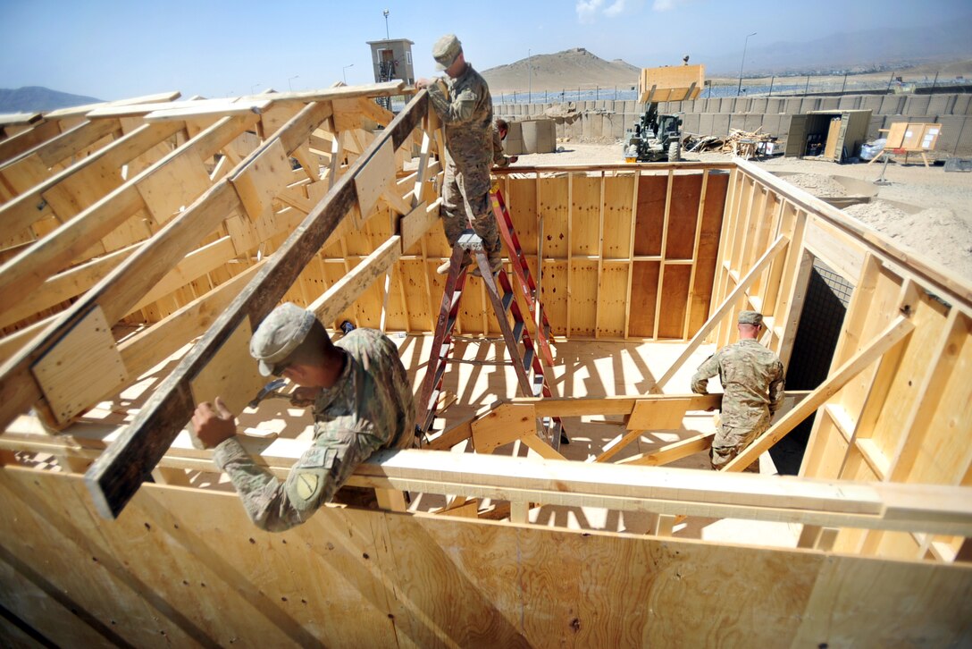 U.S. soldiers hammer a truss into place during the construction of ...