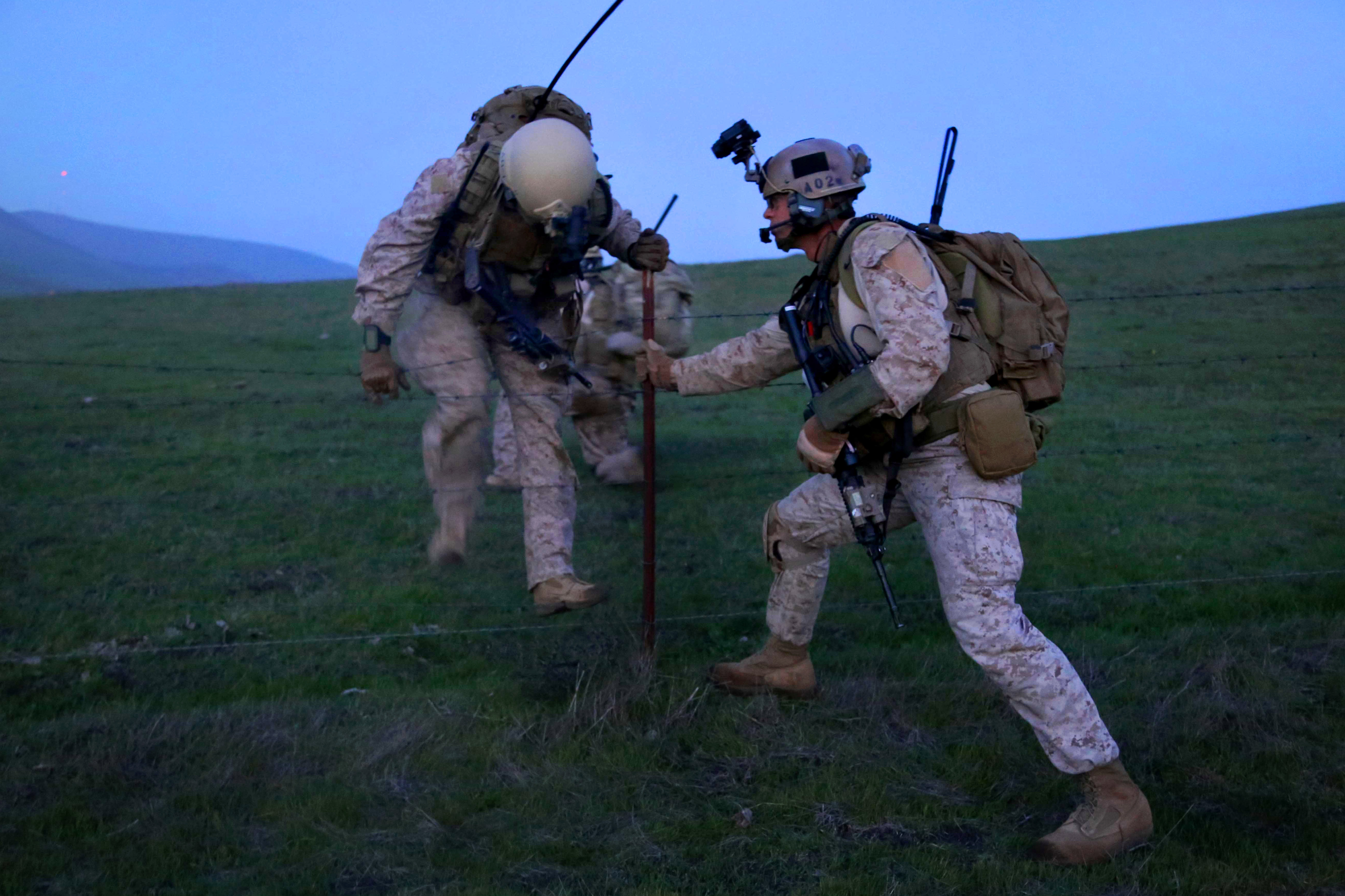 Marines climb over a barbwire fence as part of a simulated precision ...