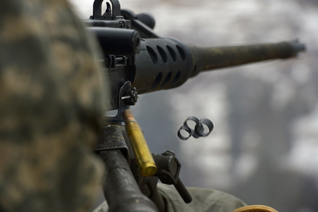 A spent brass casing and steel ammunition link eject from the side of a ...