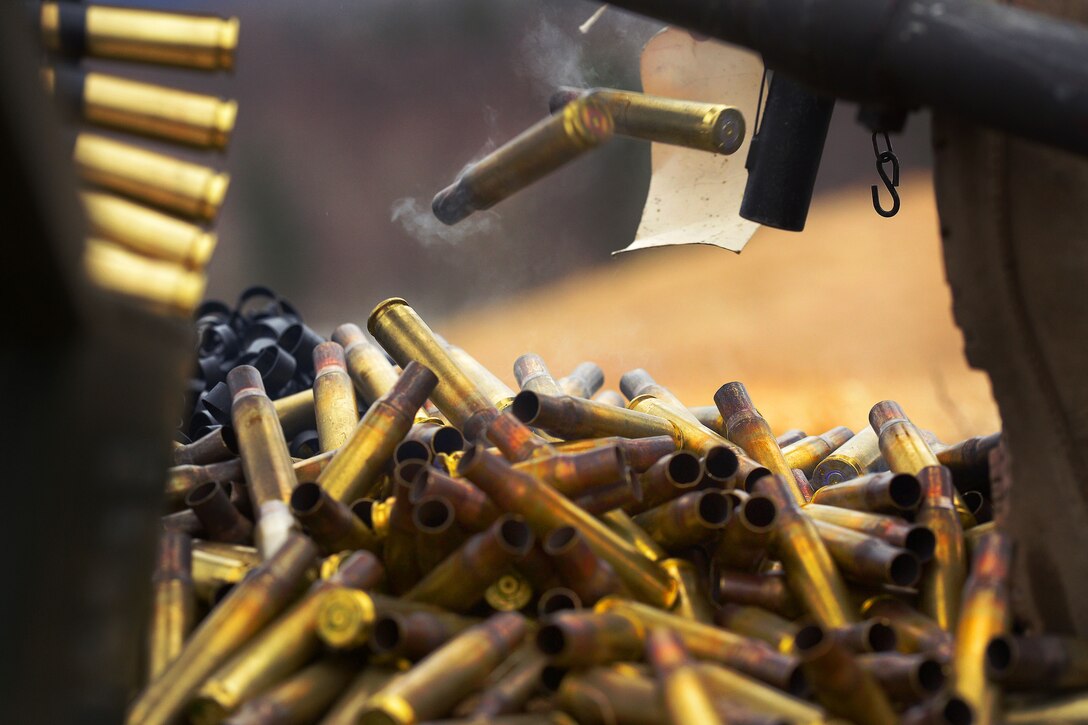 Smoking brass casings fall from the bottom of an M2A1 machine gun fired ...