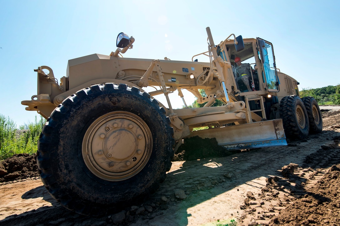 Army Sgt. Brian Guzman operates a motor grader to clear a dirt path at ...