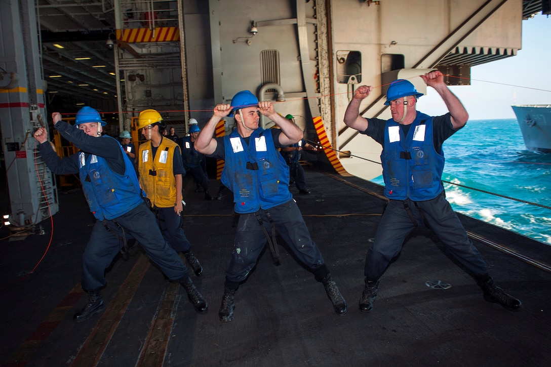 U.S. sailors heave around a line in the hangar bay of the Nimitz-class ...