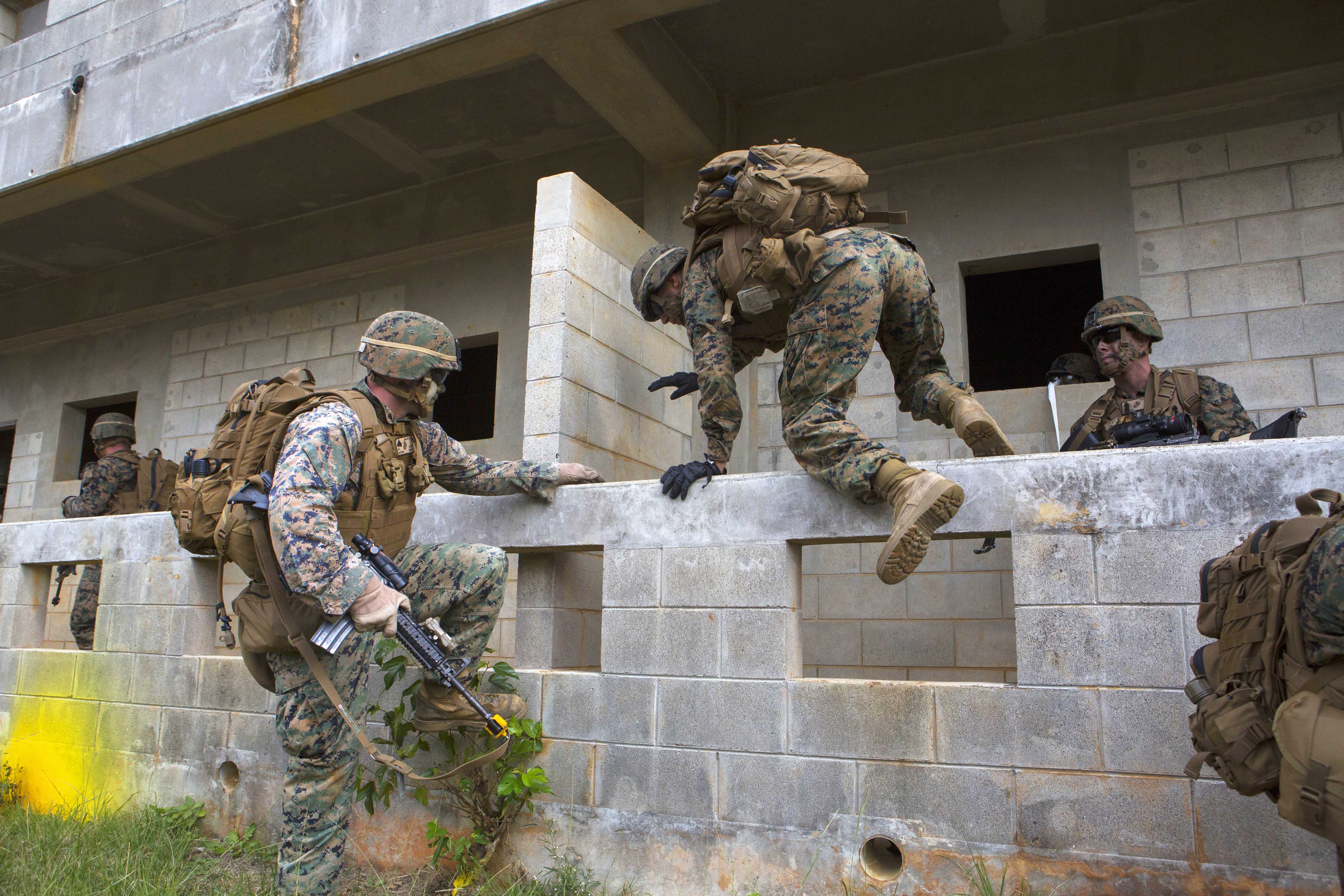 U.S. Marines jump over a wall to search a building during a vertical assault at Combat Town ...