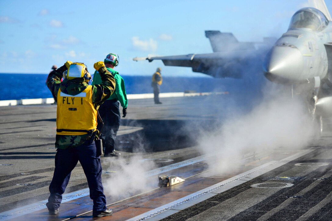 U.S. Navy Petty Officer 2nd Class Myron Aldan directs an aircraft onto ...